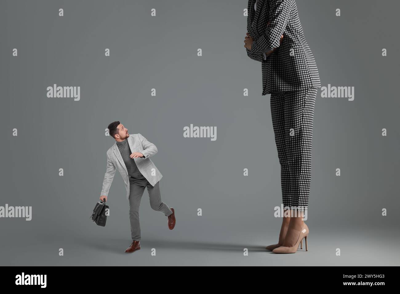 Small man running from giant woman on grey background Stock Photo - Alamy