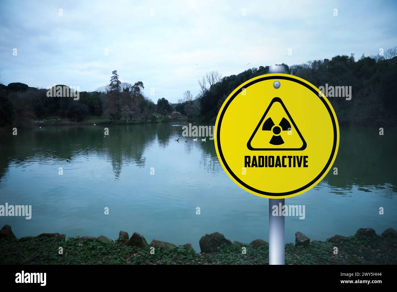 Radioactive pollution. Yellow warning sign with hazard symbol near lake ...