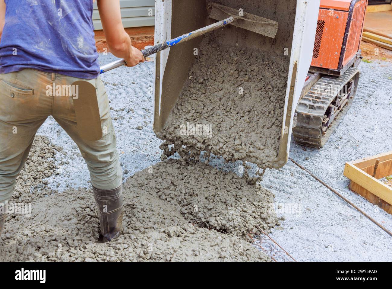 Pouring fresh cement from concrete buggy into framework in ground ...