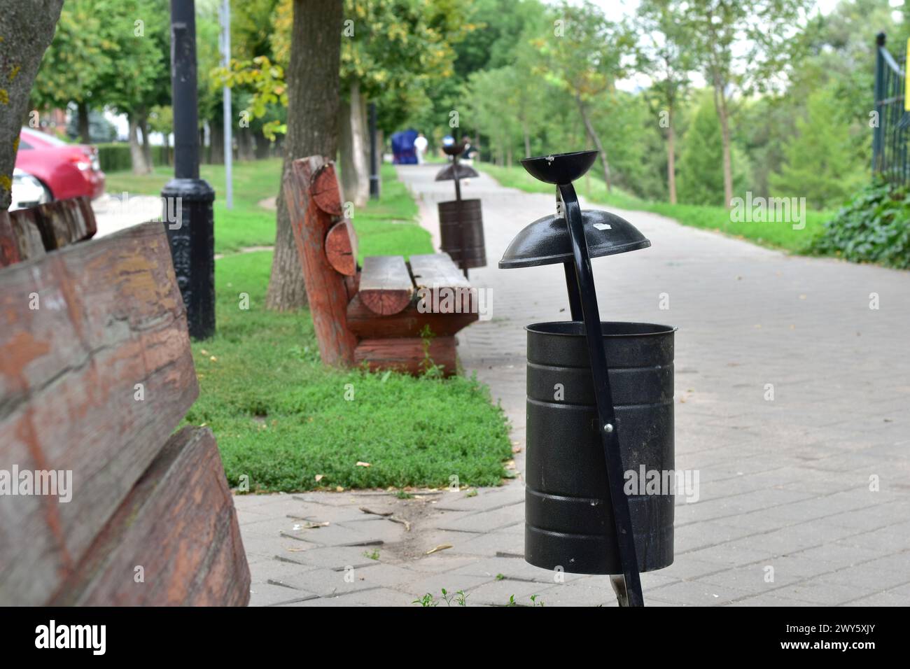 In the city park, there is a round trash can between wooden benches ...