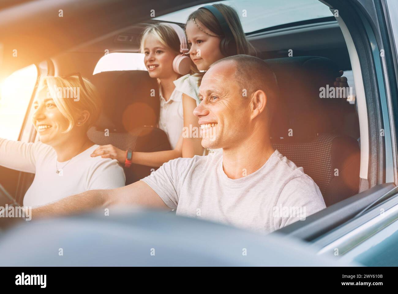 Happy smiling young couple with two daughters inside car during auto trop. They are smiling, and ...