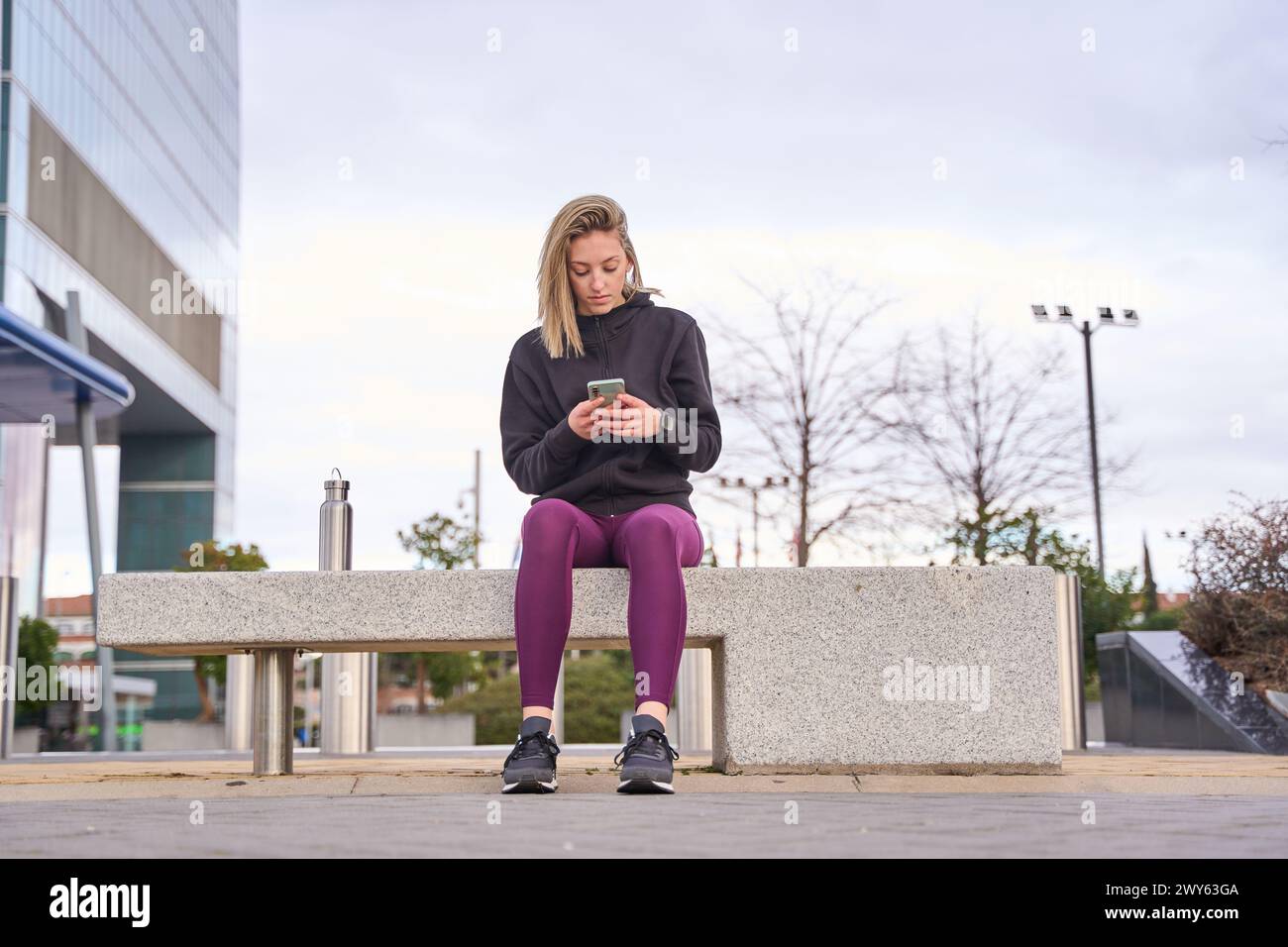 Female athlete in casual clothes sitting in training break looking at ...