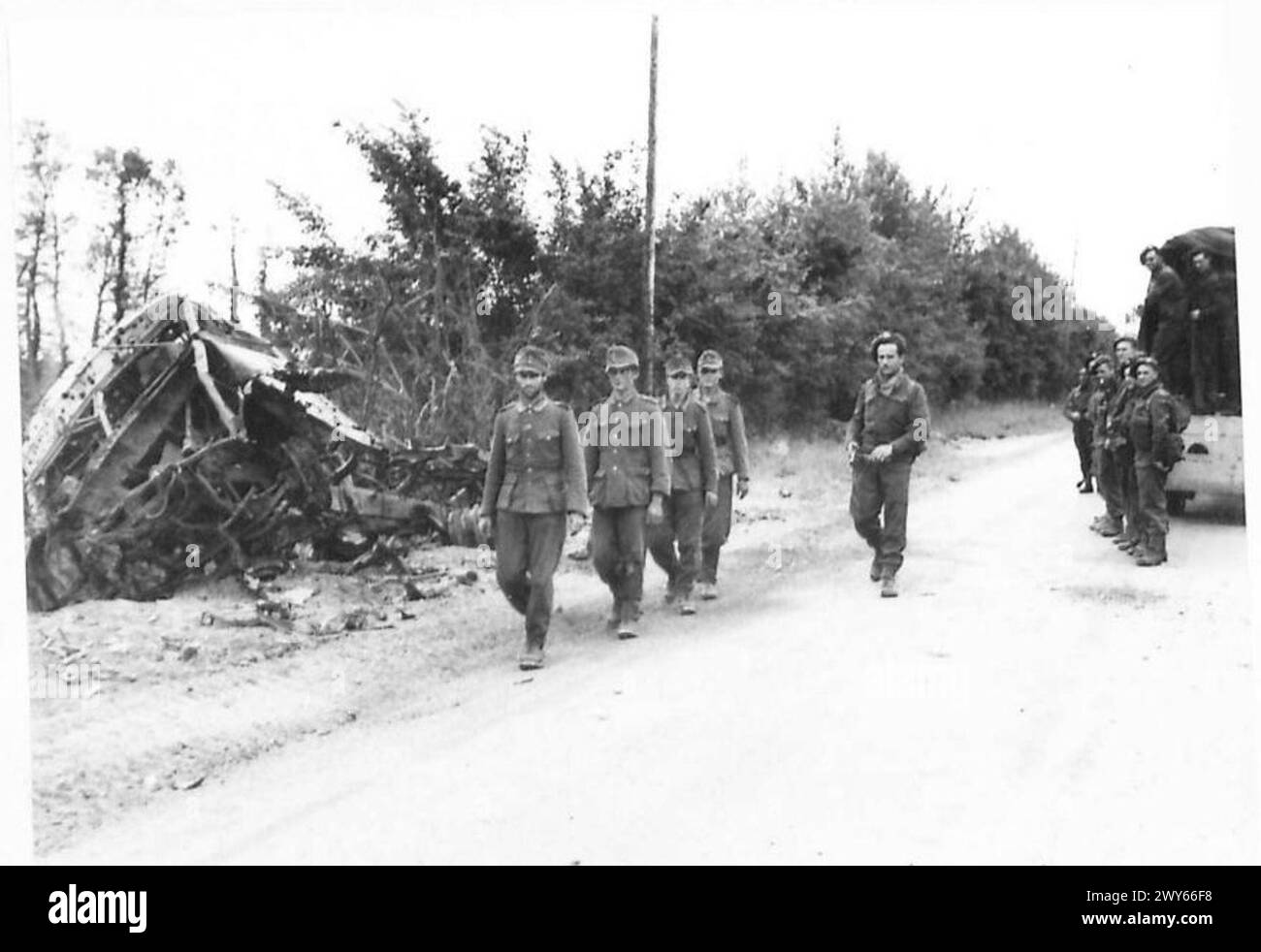 German prisoners march past a burnt-out ammunition lorry on a road near ...