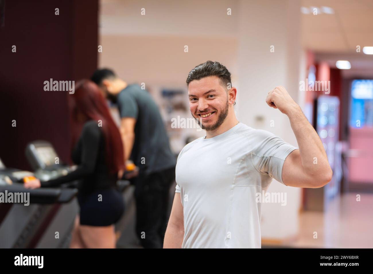 Muscular man in white tee flexes his bicep, with focused gym-goers ...