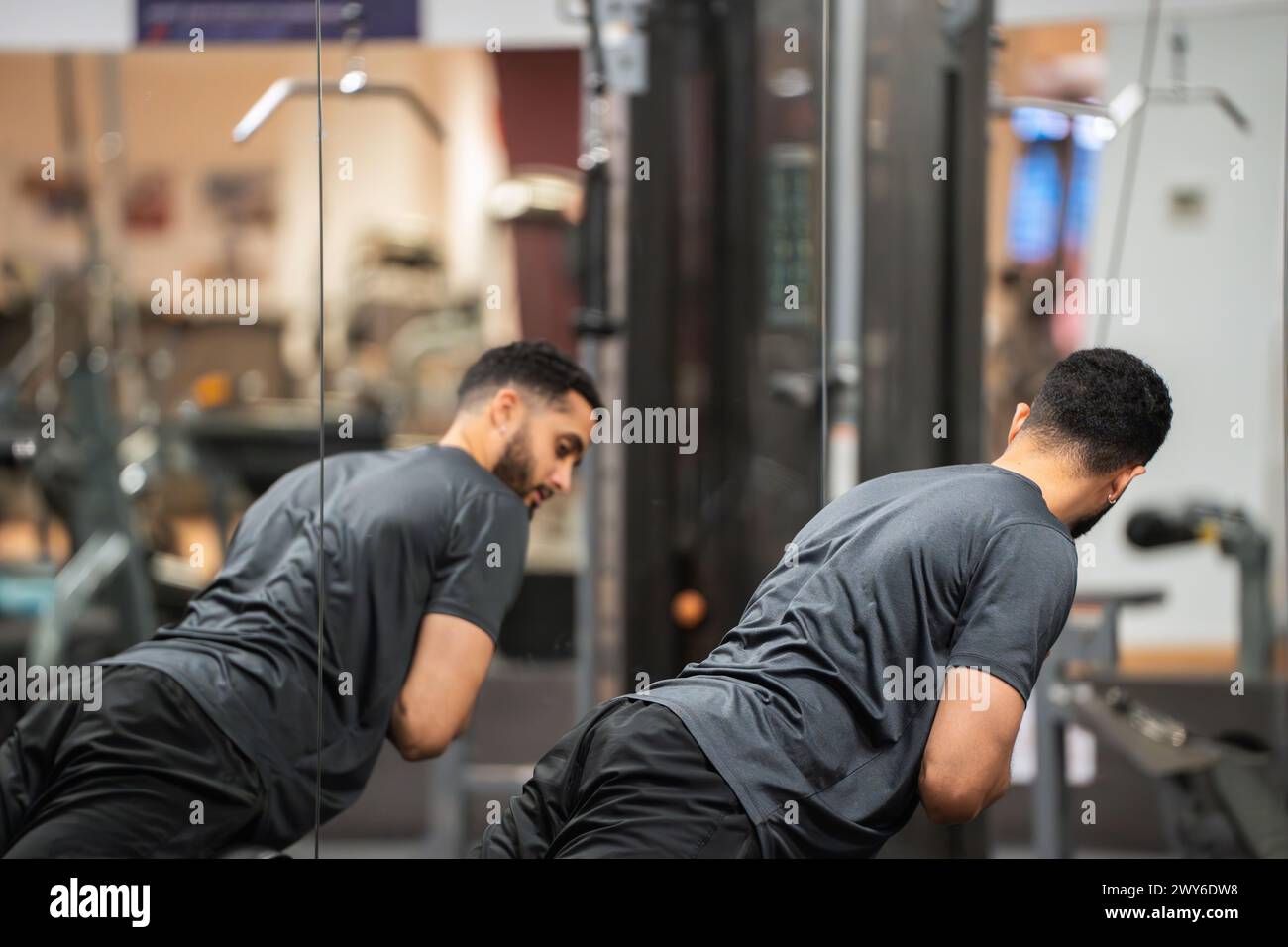 Concentrated man using back extension machine at gym, with a mirror ...
