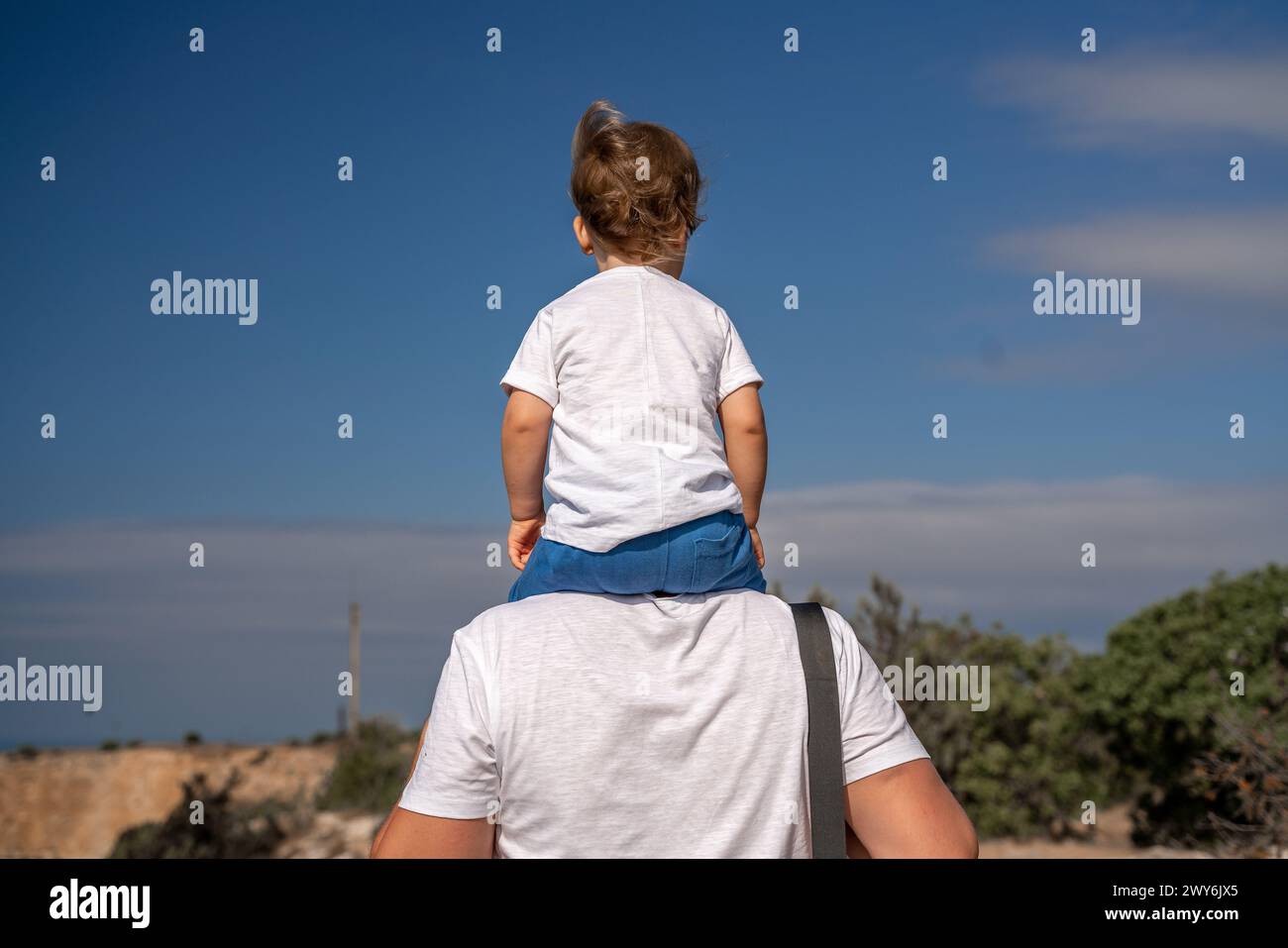 man is carrying a child on his back. The child is wearing a white shirt ...