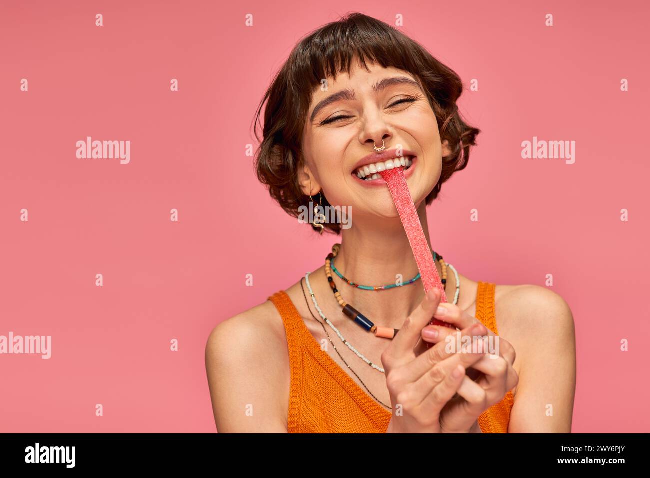 excited and young woman with nose piercing biting sweet and sour candy ...