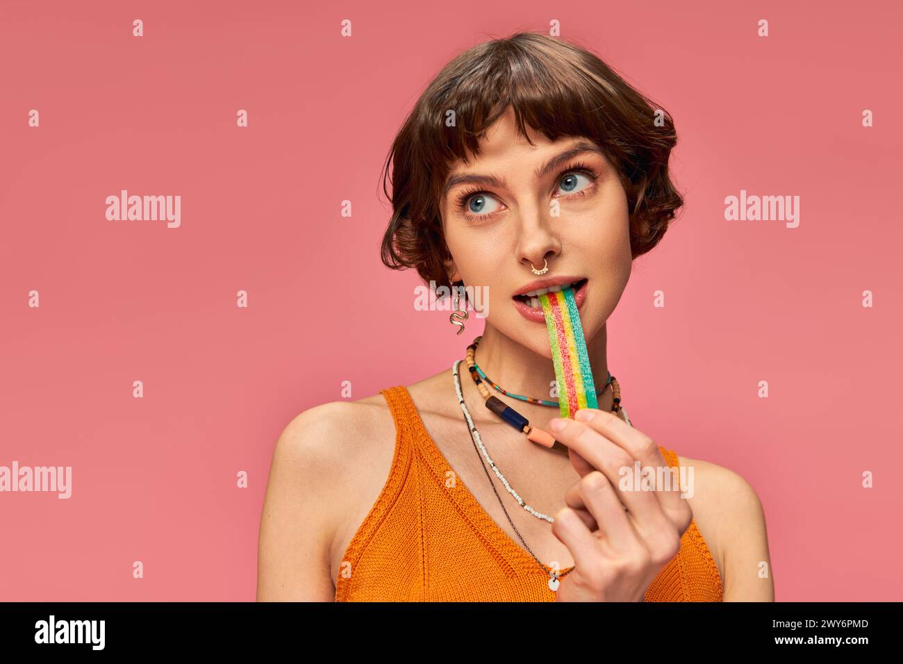 portrait of playful young woman in her 20s biting sweet and sour candy ...