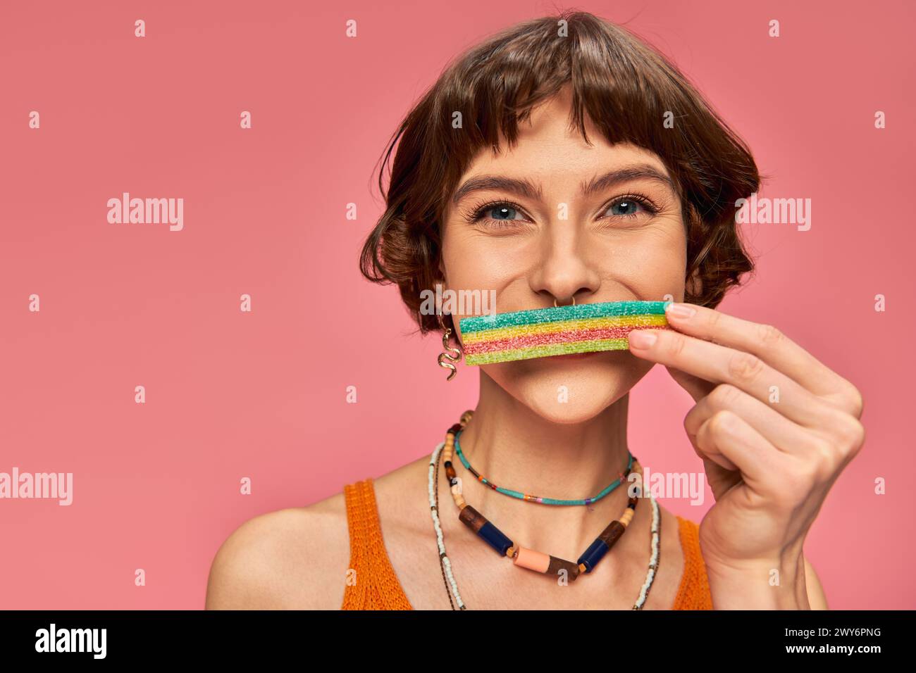 portrait of woman in her 20s covering lips with sweet and sour candy ...