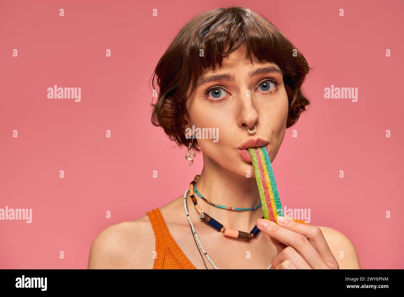 portrait of playful woman in her 20s biting sweet and sour candy strip ...
