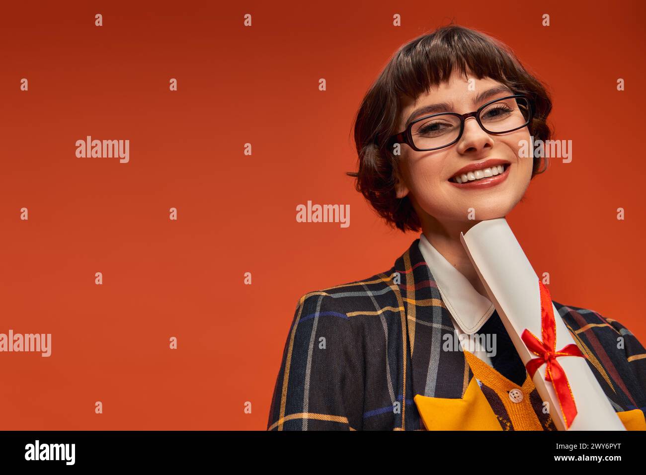 positive college girl in uniform and glasses holding her graduation ...