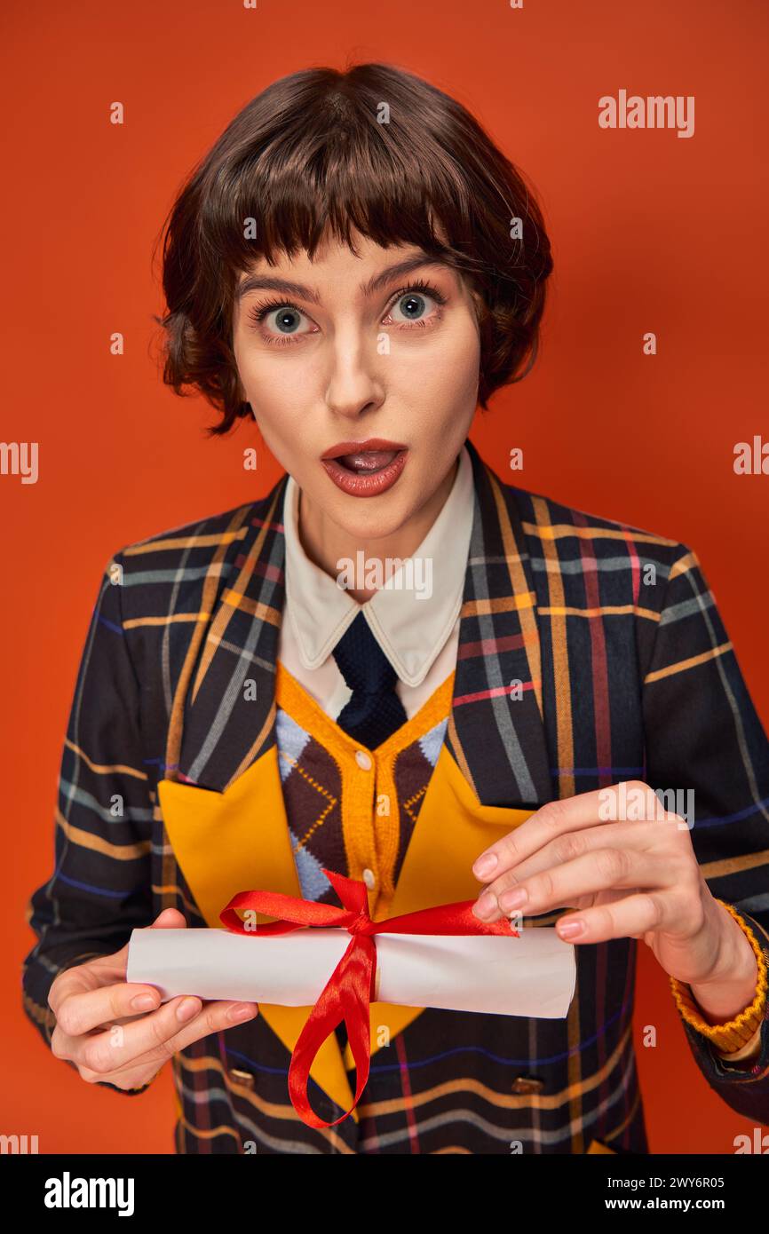 portrait of shocked college girl in checkered uniform holding ...