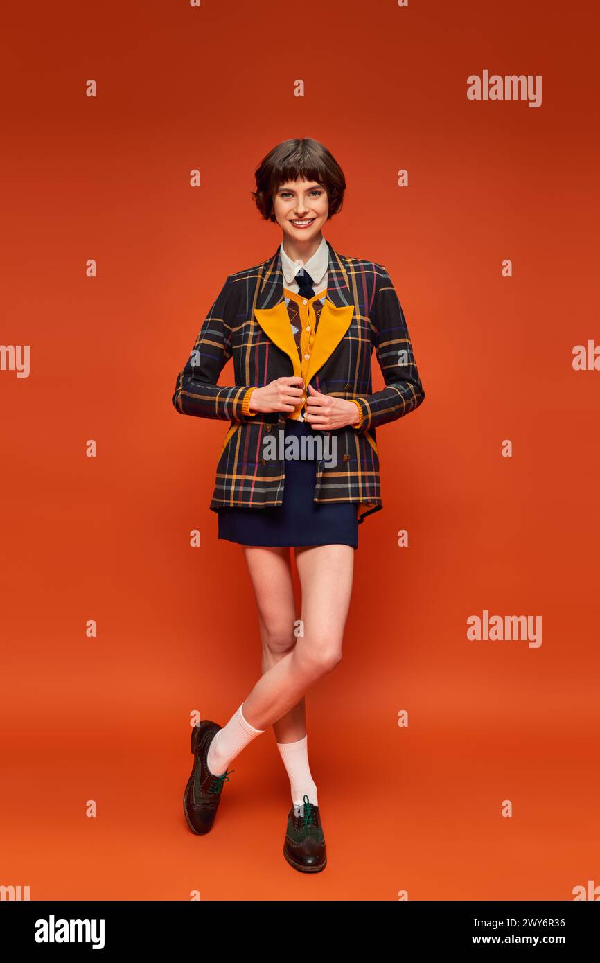 full length of stylish student in checkered blazer and skirt on orange ...