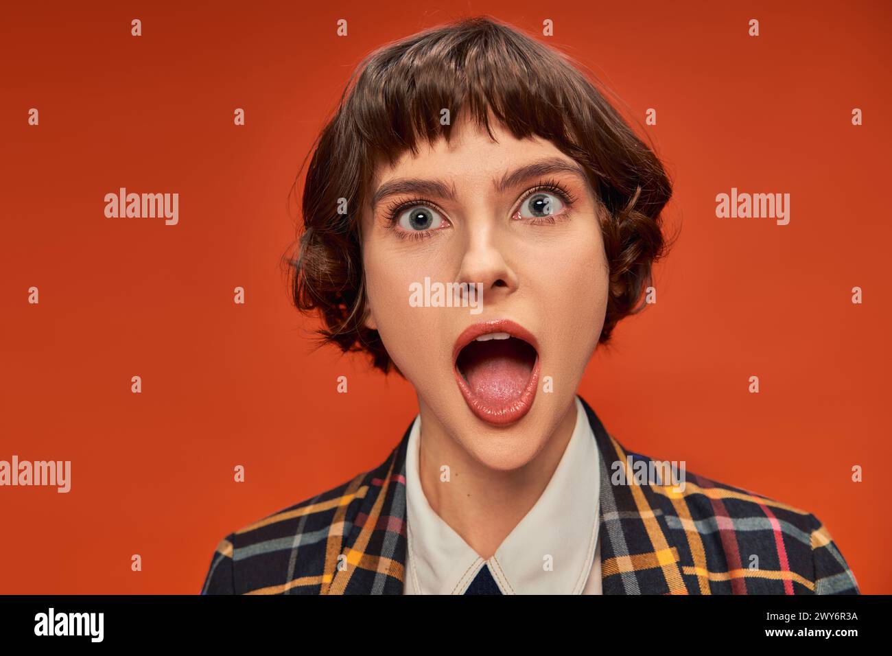Surprised college girl looking at camera with wide eyes on orange ...