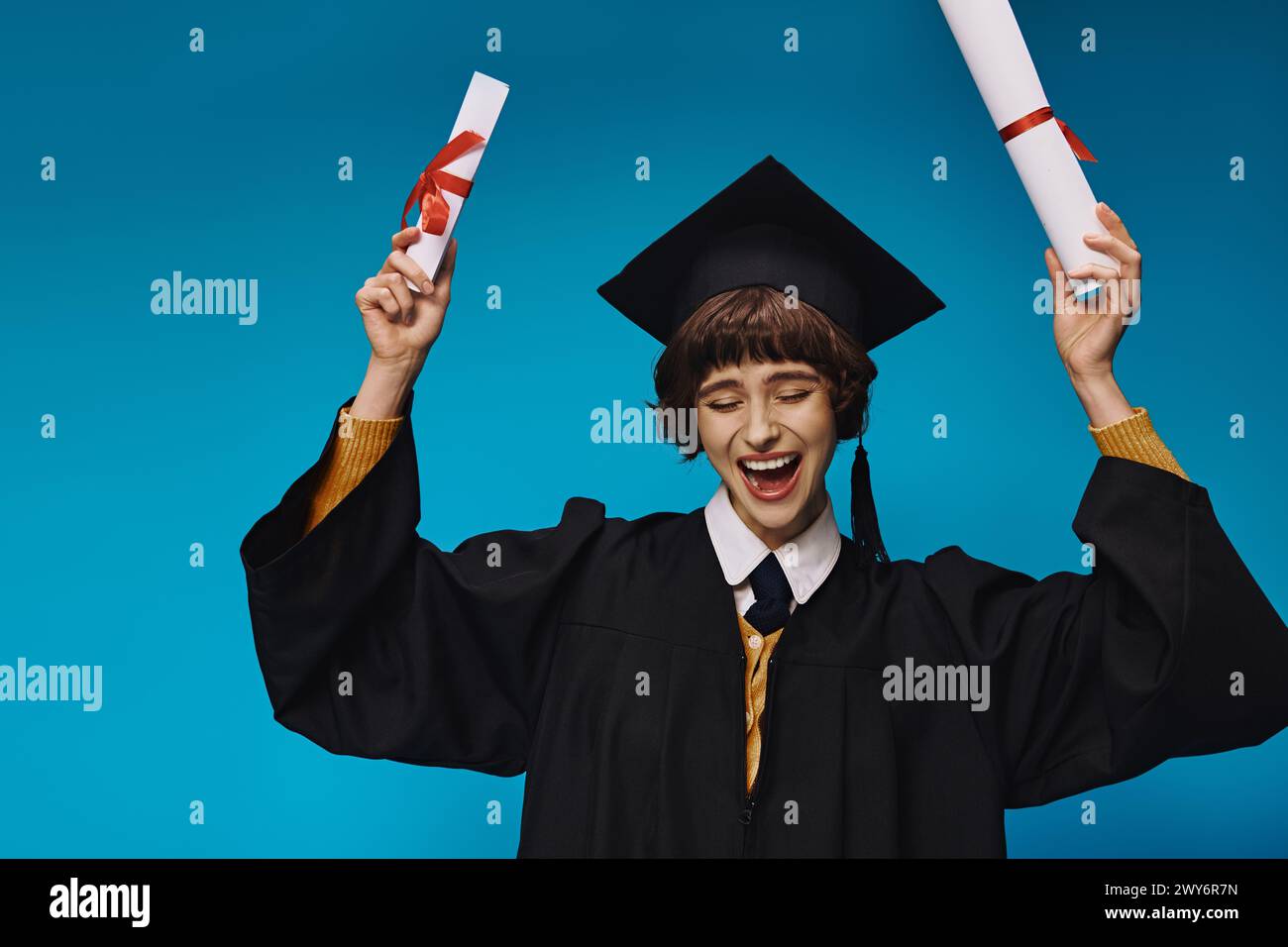 Eager grad college girl in gown and academic cap holding diplomas with ...