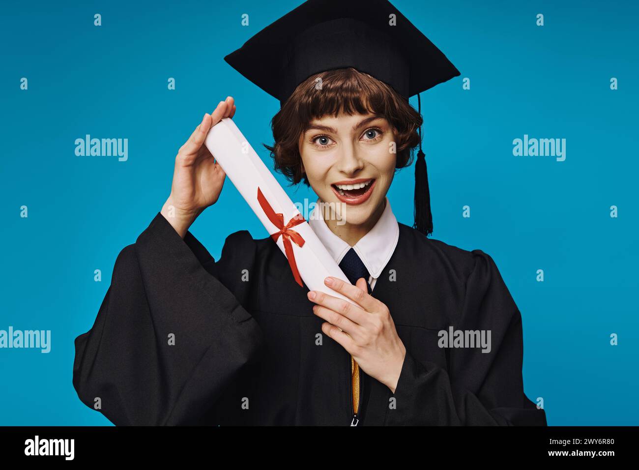 cheerful college girl in gown and academic cap holding her diploma with ...