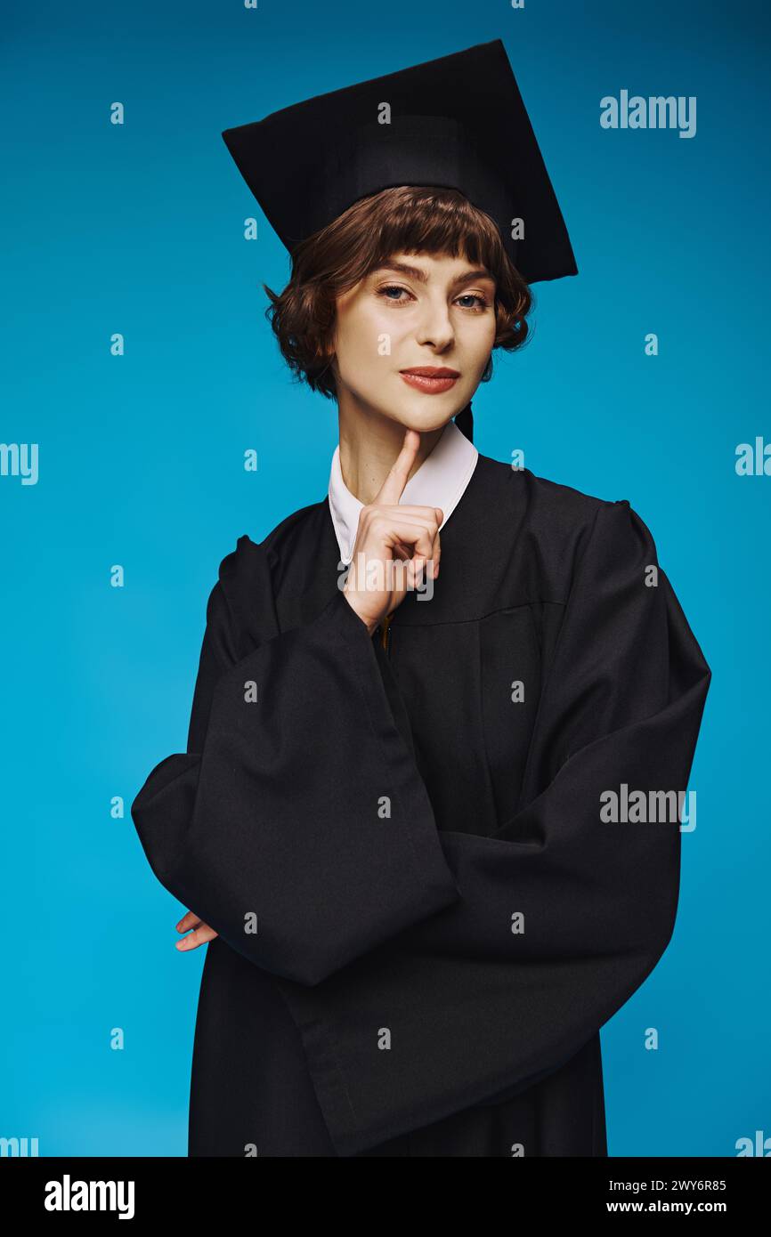 young graduated college girl in gown and cap standing on blue ...