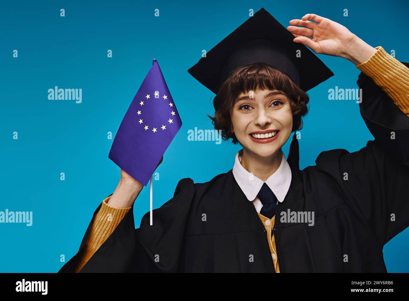 graduated girl in gown and cap holding EU flag and smiling on blue ...