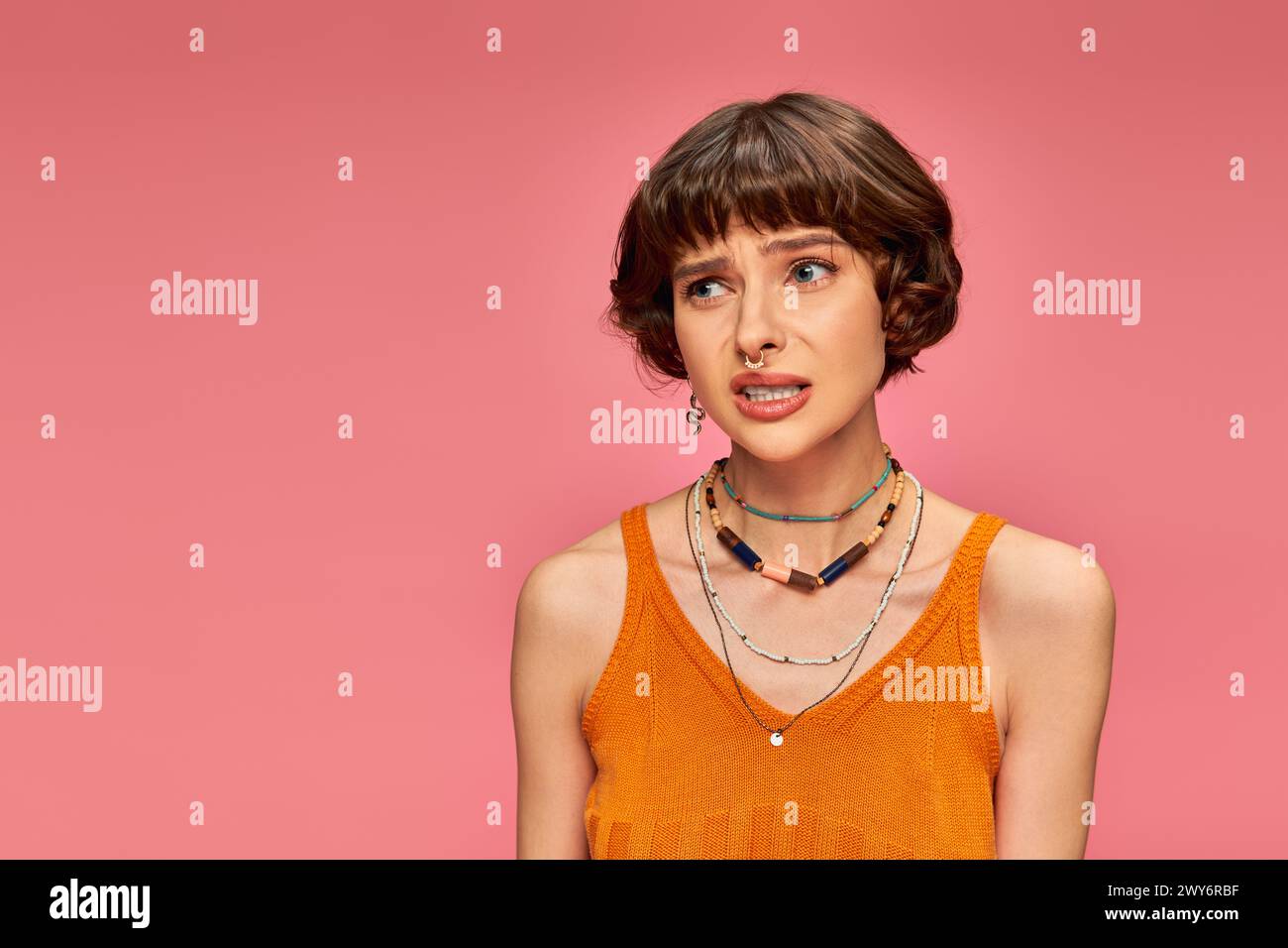 puzzled young woman in her 20s standing in orange knitted tank top on ...