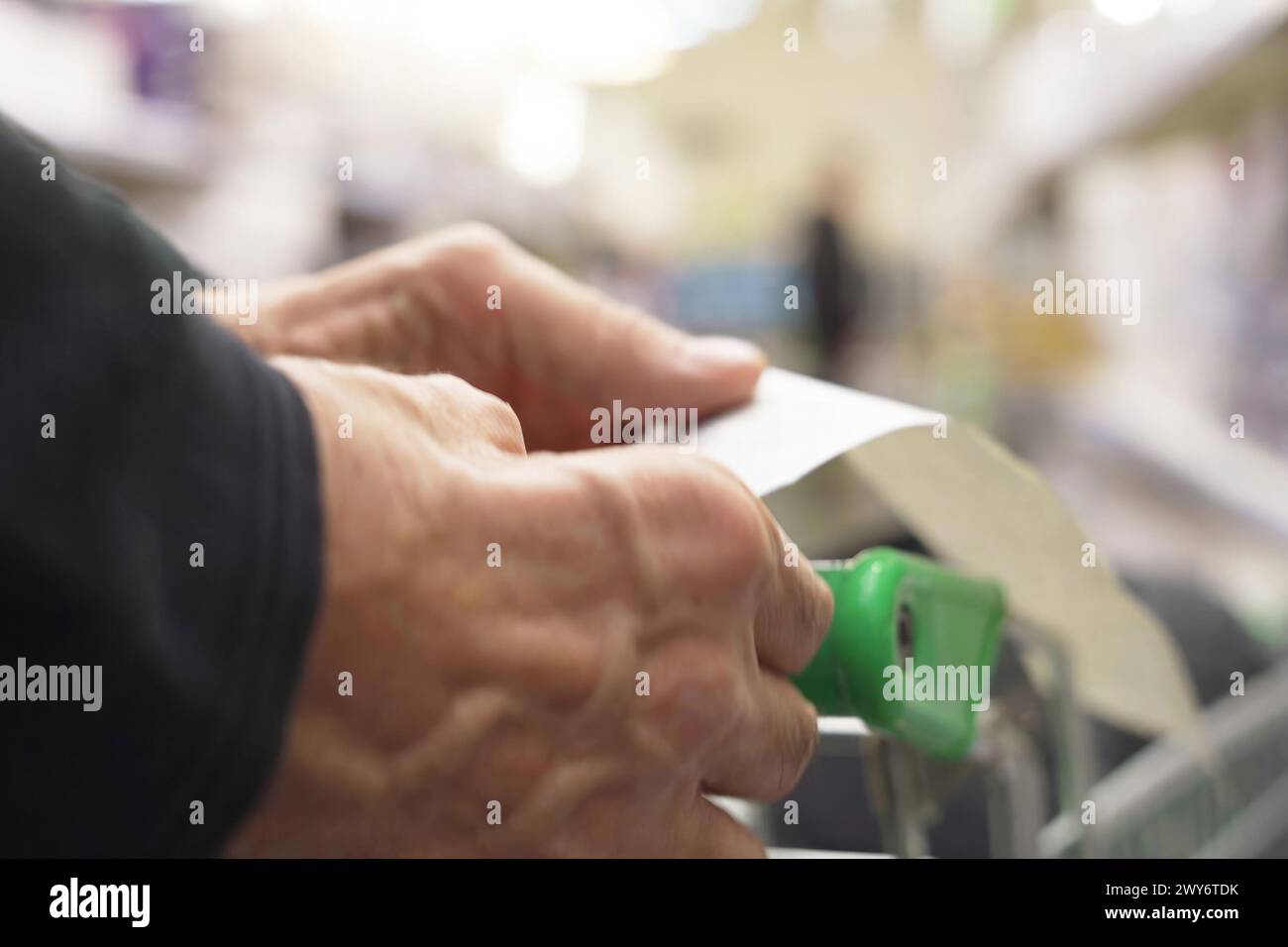 The hands of an unrecognizable older man hold a sales receipt next to a ...