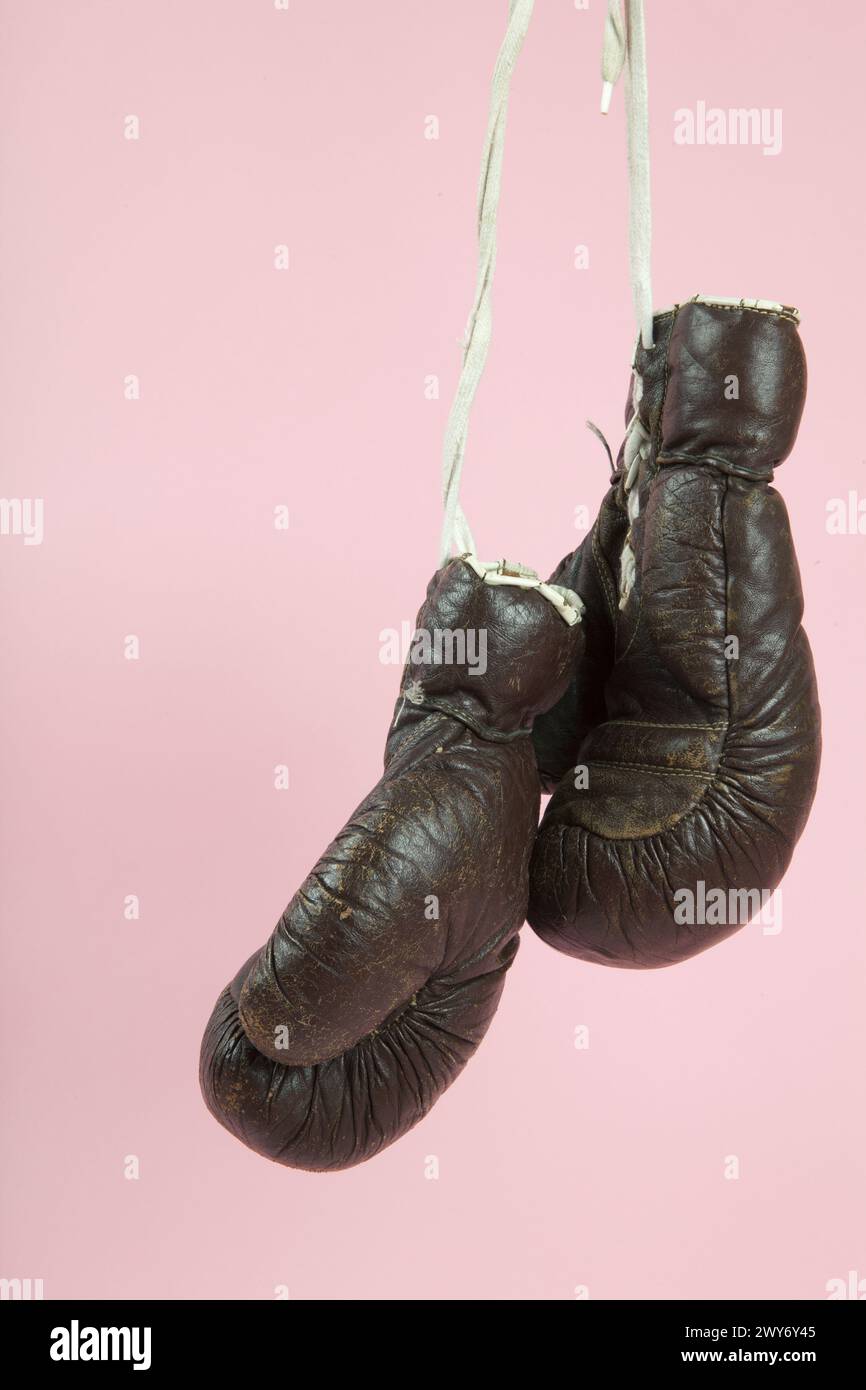 a pair of old boxing gloves hung in front of a candy-pink background ...