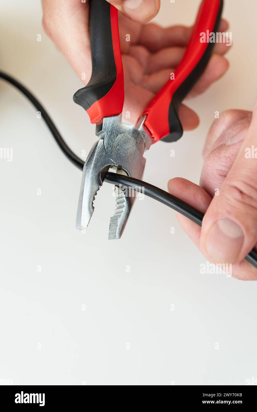 Close-up of hands using red and black pliers to cut a black cable on a ...