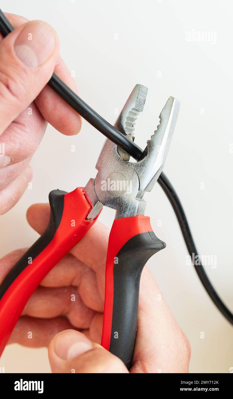 Close-up of hands using pliers to cut a black wire, highlighting a DIY ...
