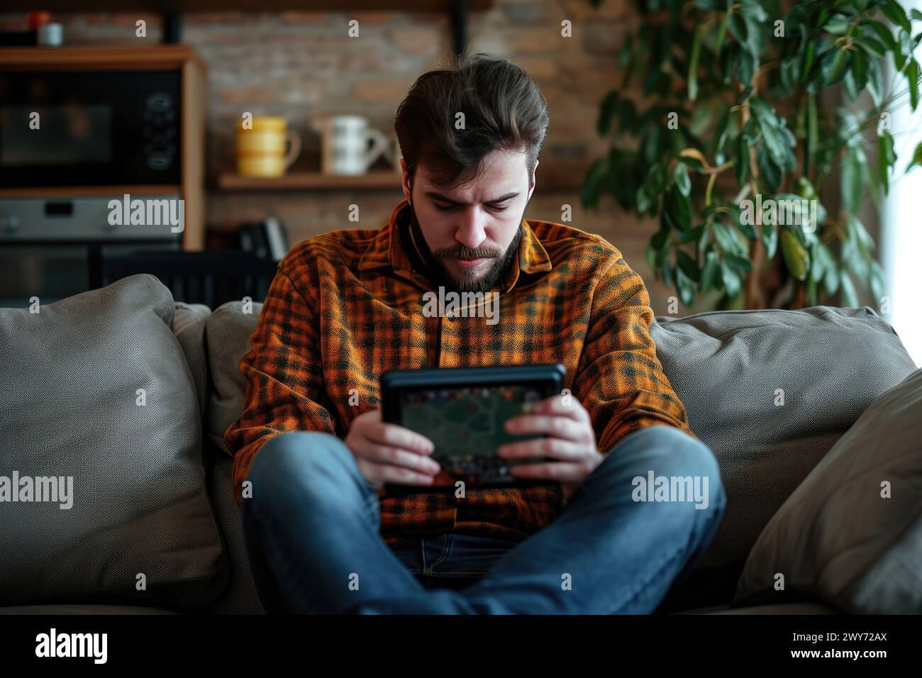 A man sitting comfortably on a couch and engaging with a tablet device ...