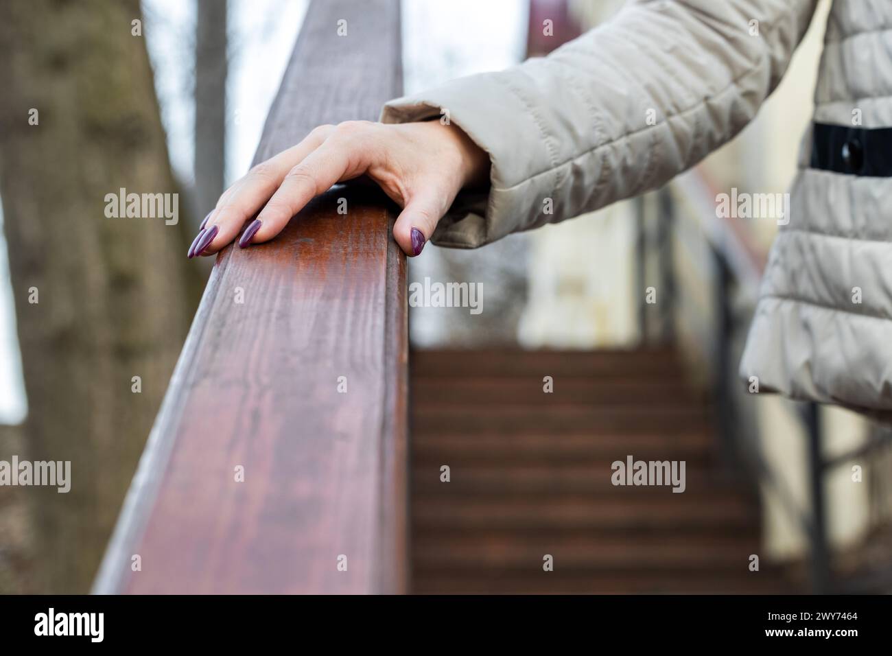 woman holding on to wooden railing going down the stairs. hand holding ...