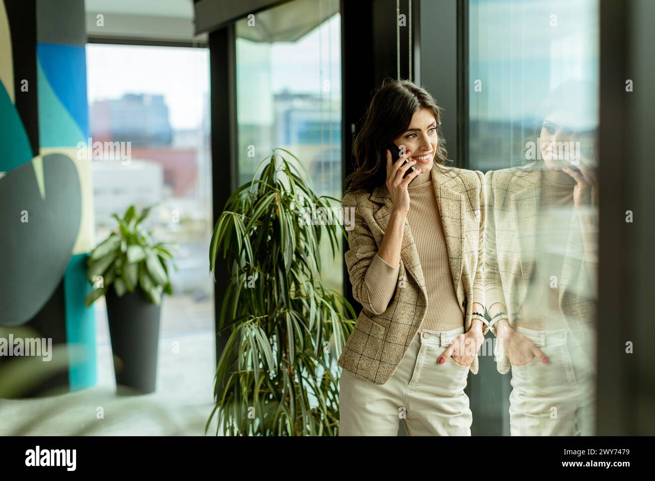 Contemplative woman using mobile phone and gazes out of a window, with ...