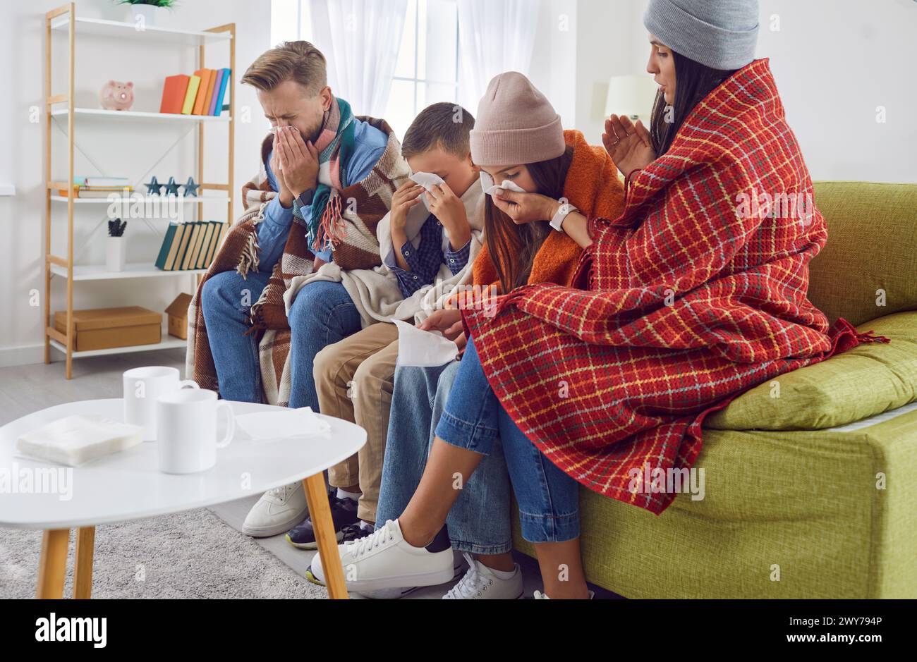Sick mother, father and children sitting on couch, holding tissues ...