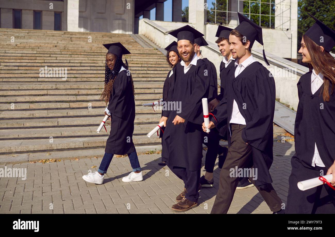 Group of happy diverse university graduates walking about campus on ...