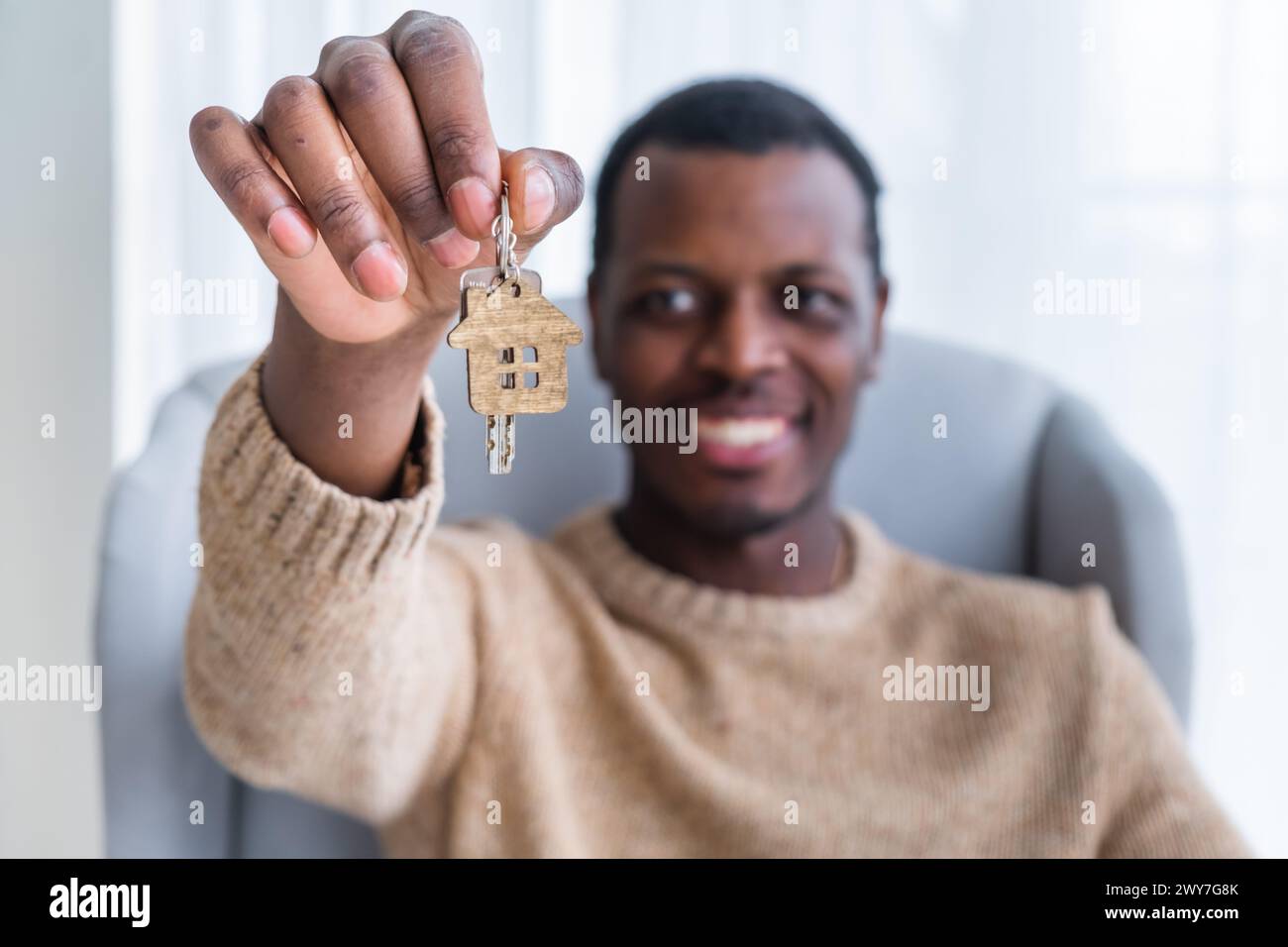 A cheerful man proudly presents a set of keys with a house-shaped ...