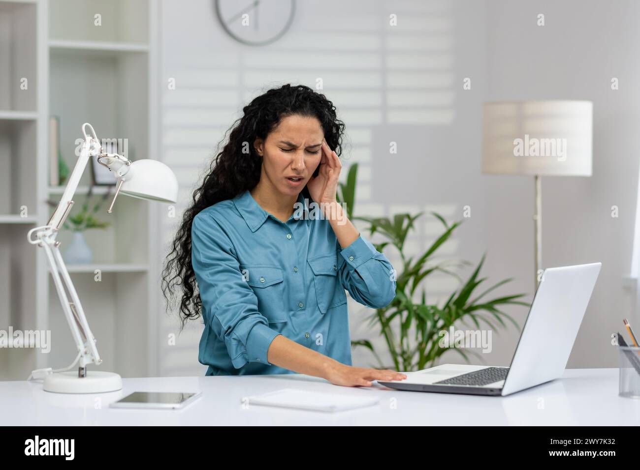 A distressed Hispanic woman is holding her ear in pain while working at ...