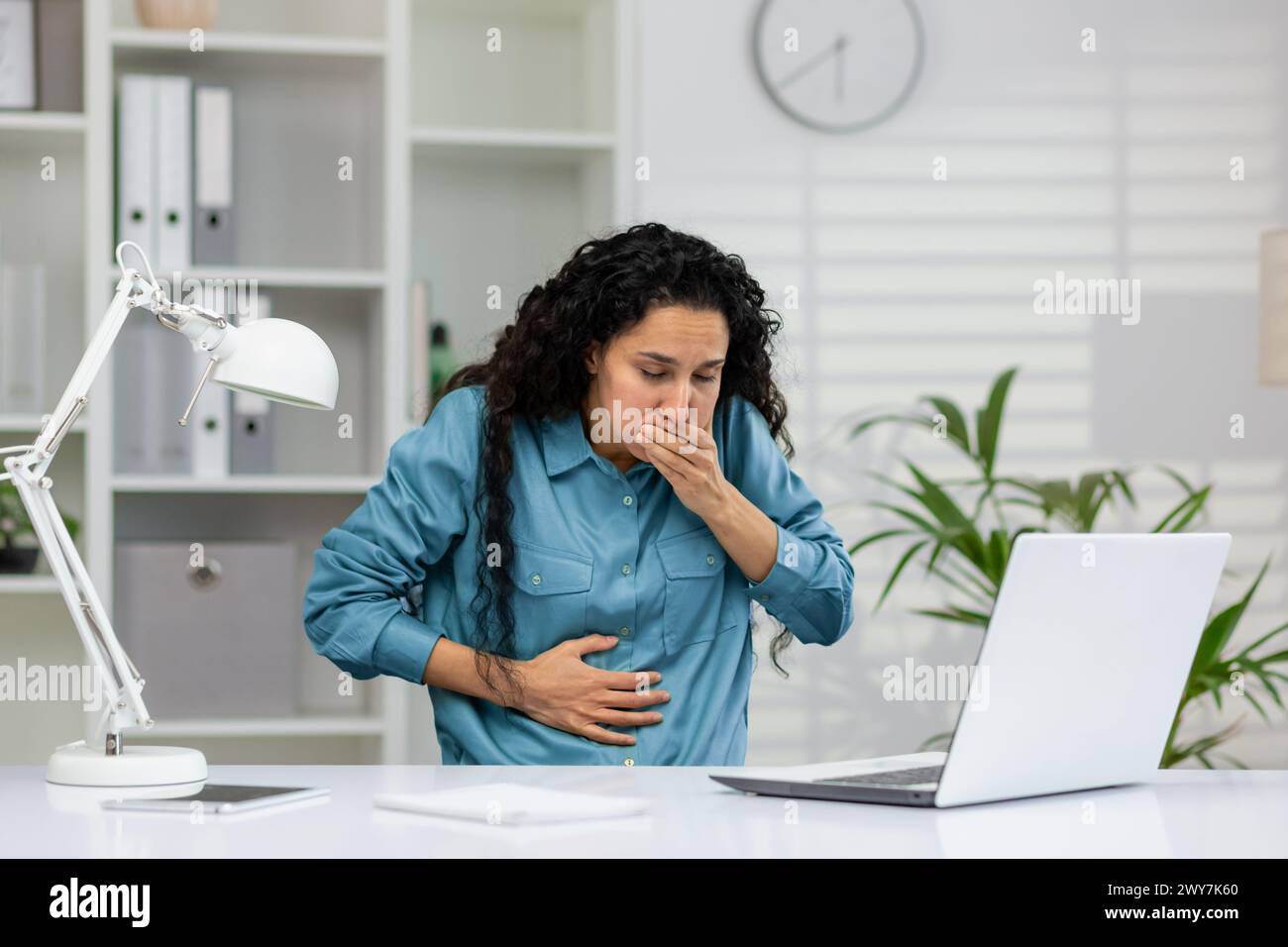 An adult woman experiencing nausea at her desk with a hand over her ...