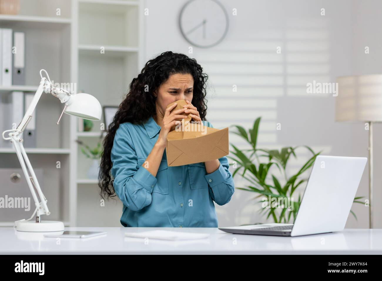 A distressed businesswoman in a blue shirt is breathing into a paper ...