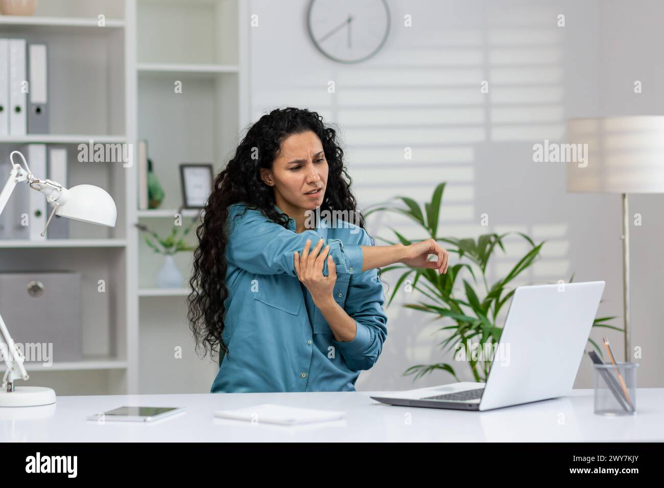 Professional woman at work grimacing in pain while clutching her elbow ...