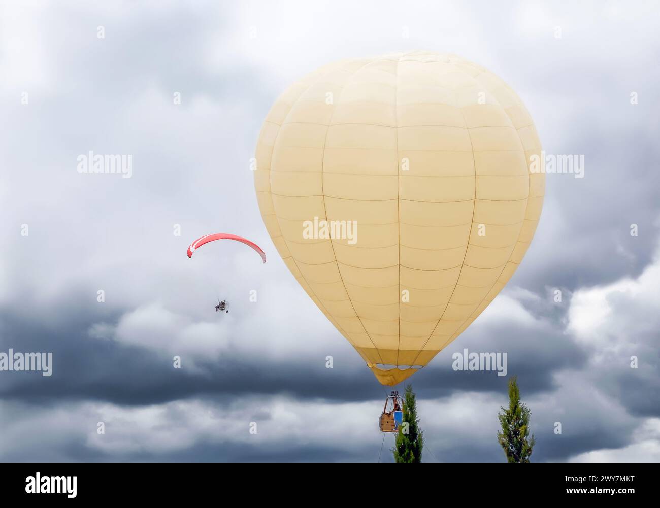 Large hot air balloon flying in the sky with clouds next to a paramotor ...