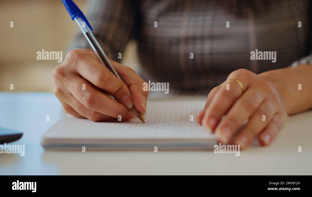 Teleworker at desk transcribing data from laptop to notepad, finalizing ...