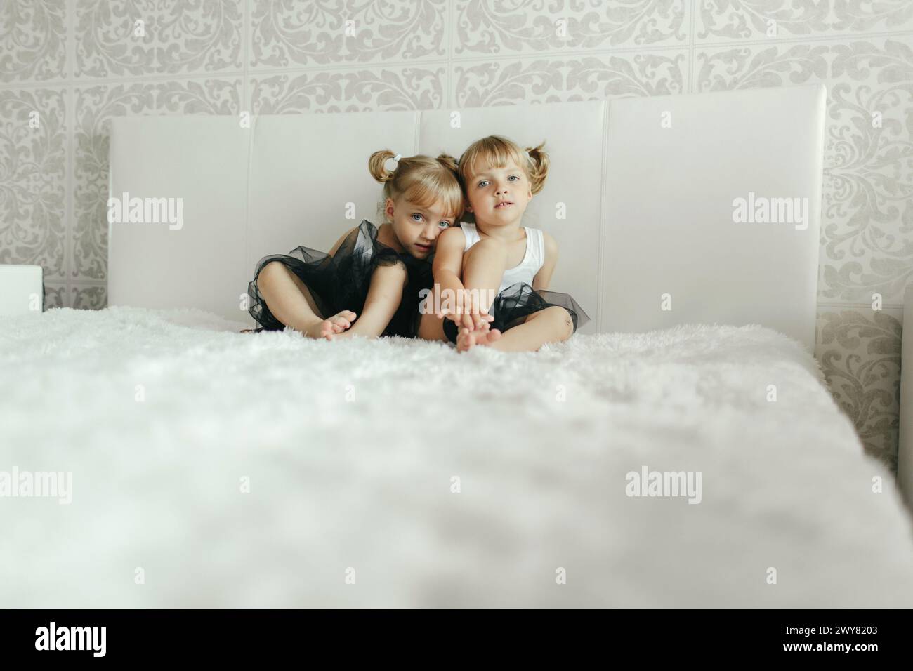 Two young girls, sitting closely side by side on a bed, engaging in a ...