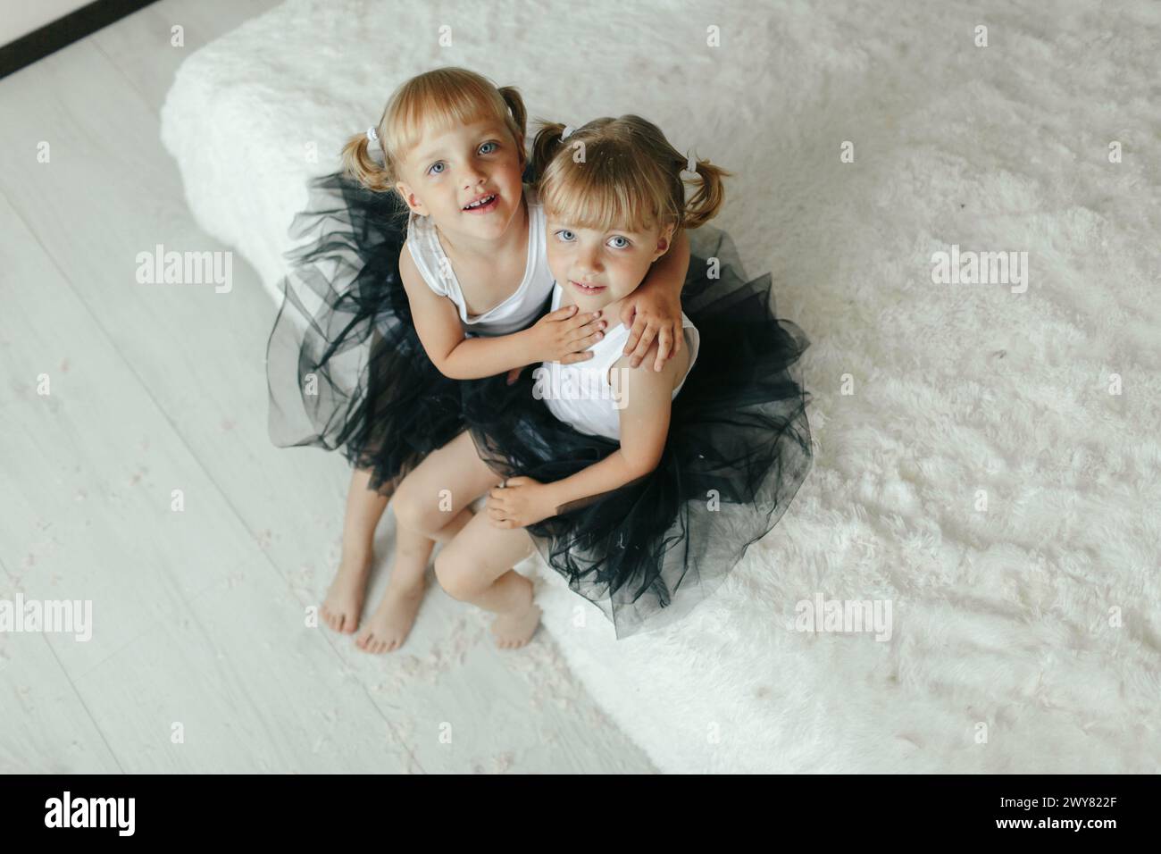 Two young girls, sitting closely together on a bed, look at something ...