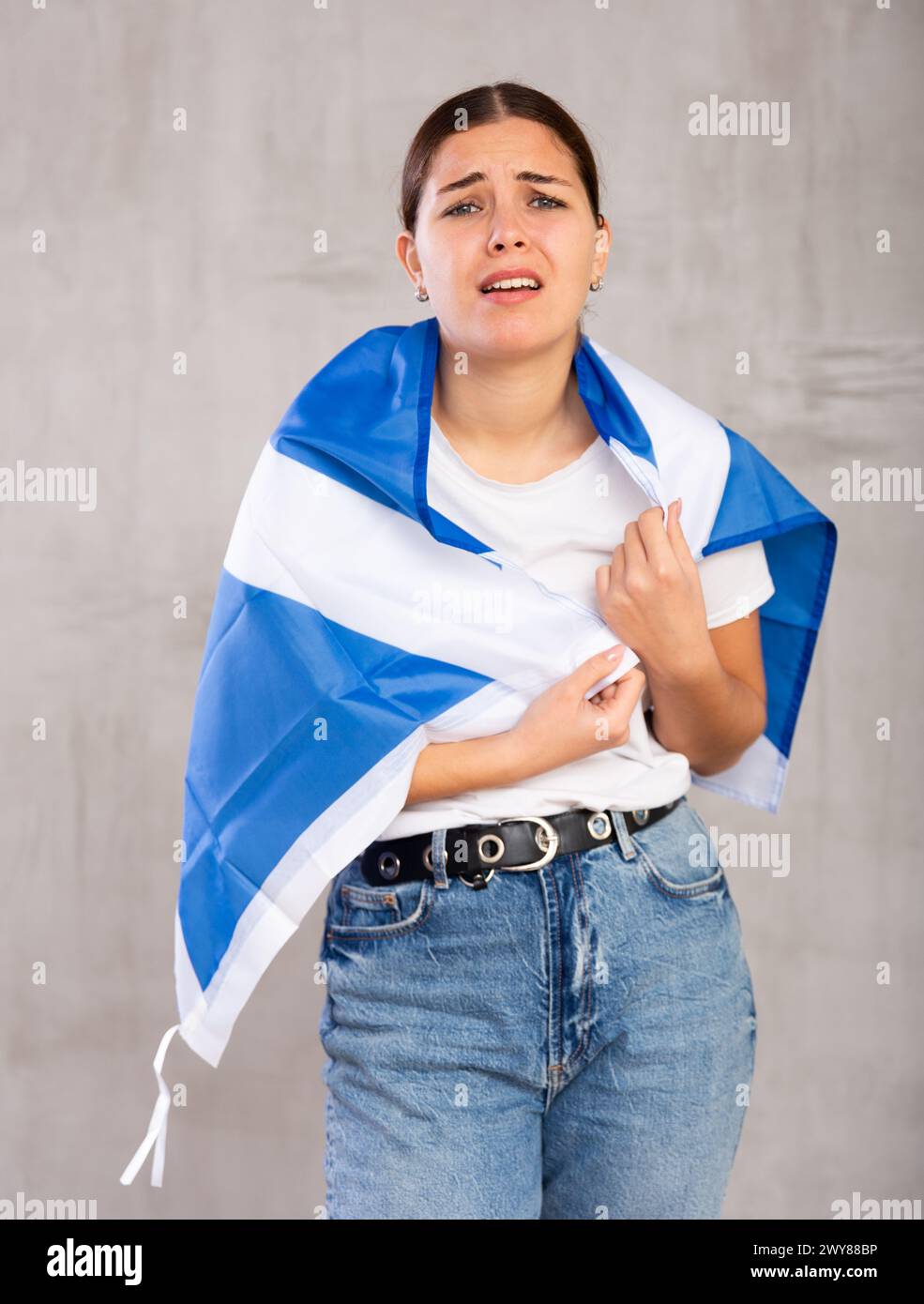 Sad young woman holding Scotland flag against unicoloured background ...