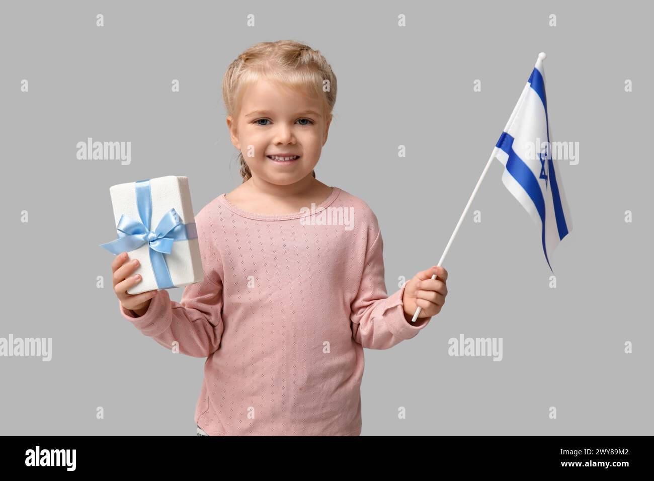 Cute happy little girl with Israel flag and gift box on grey background ...