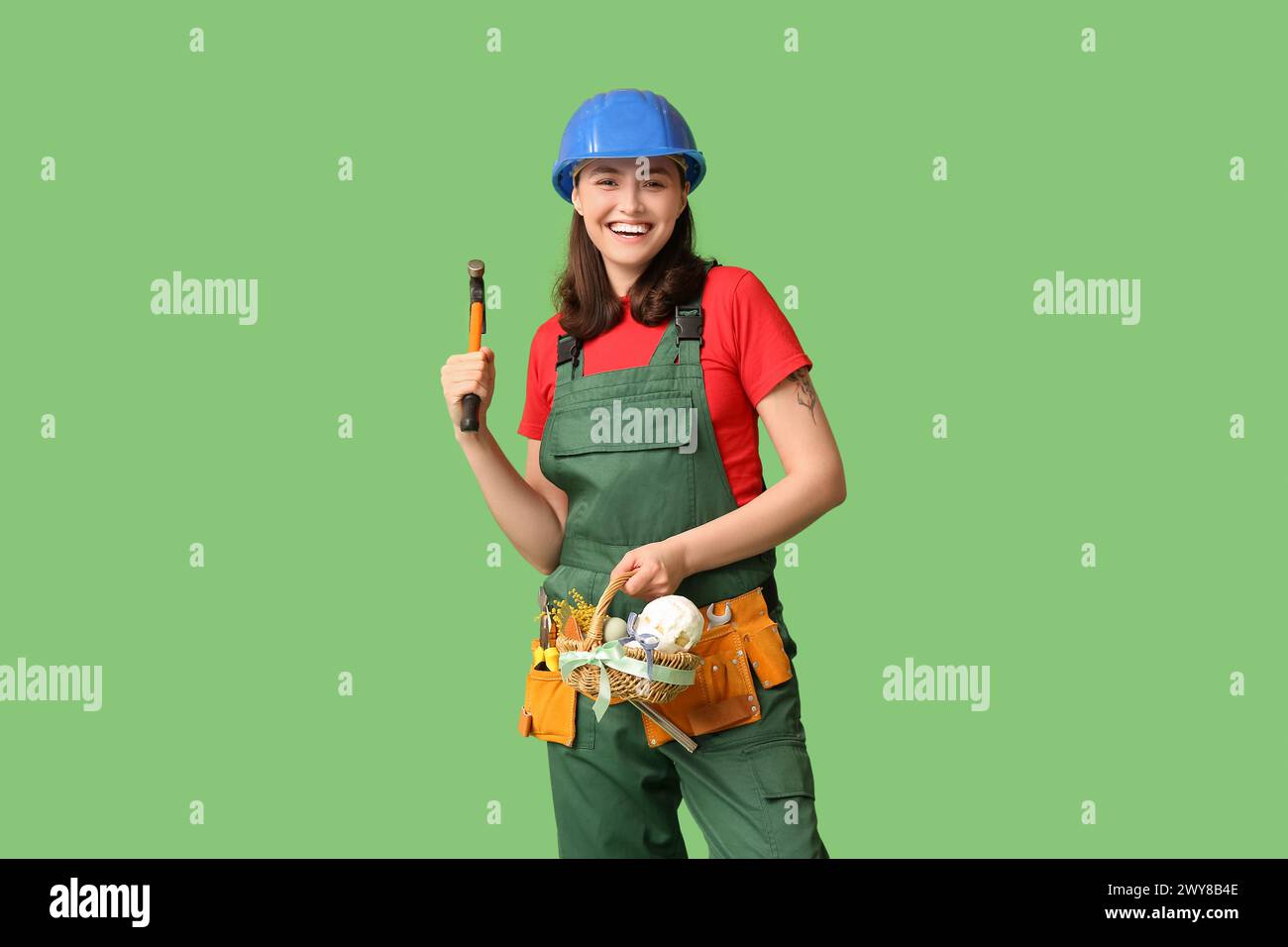 Happy female builder with Easter basket, hammer and tools on green ...