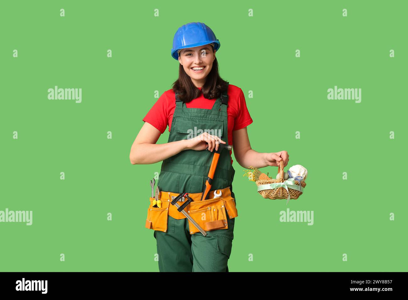 Happy female builder with Easter basket, hammer and tools on green ...