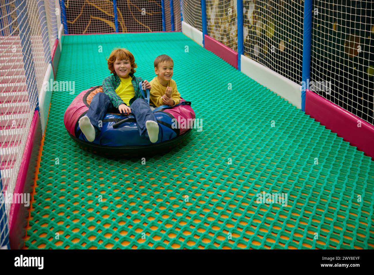 Happy children enjoying tuba ride down on slide at indoor kids ...