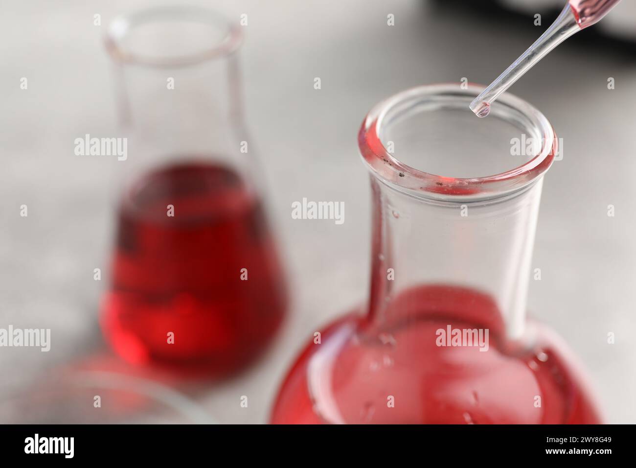 Laboratory analysis. Dripping red liquid into flask at light grey table ...