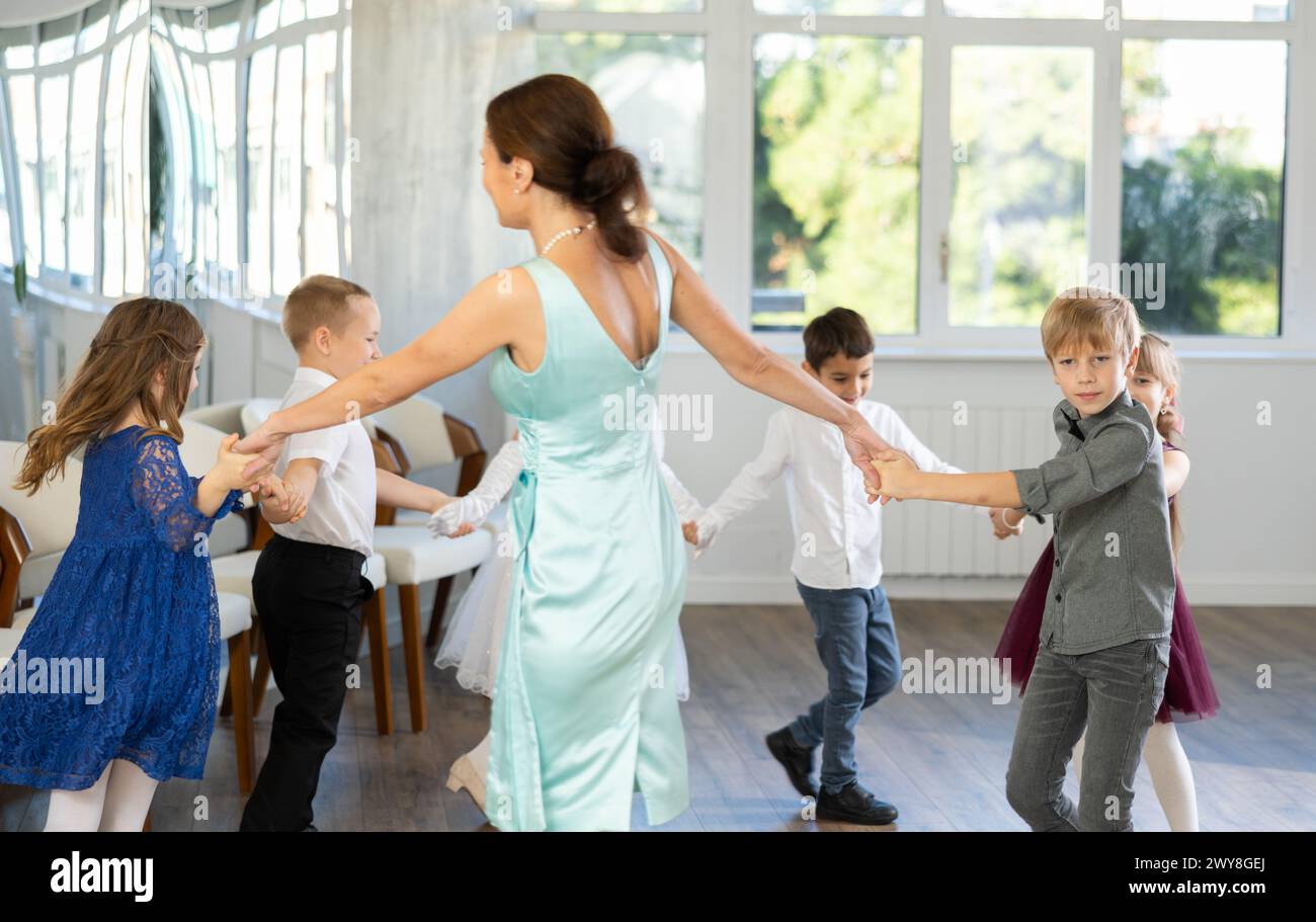Little children in elegant dresses doing round dance in school hall ...