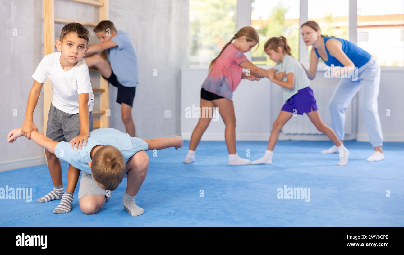 Children practicing in pair self-defence movements with female trainer ...