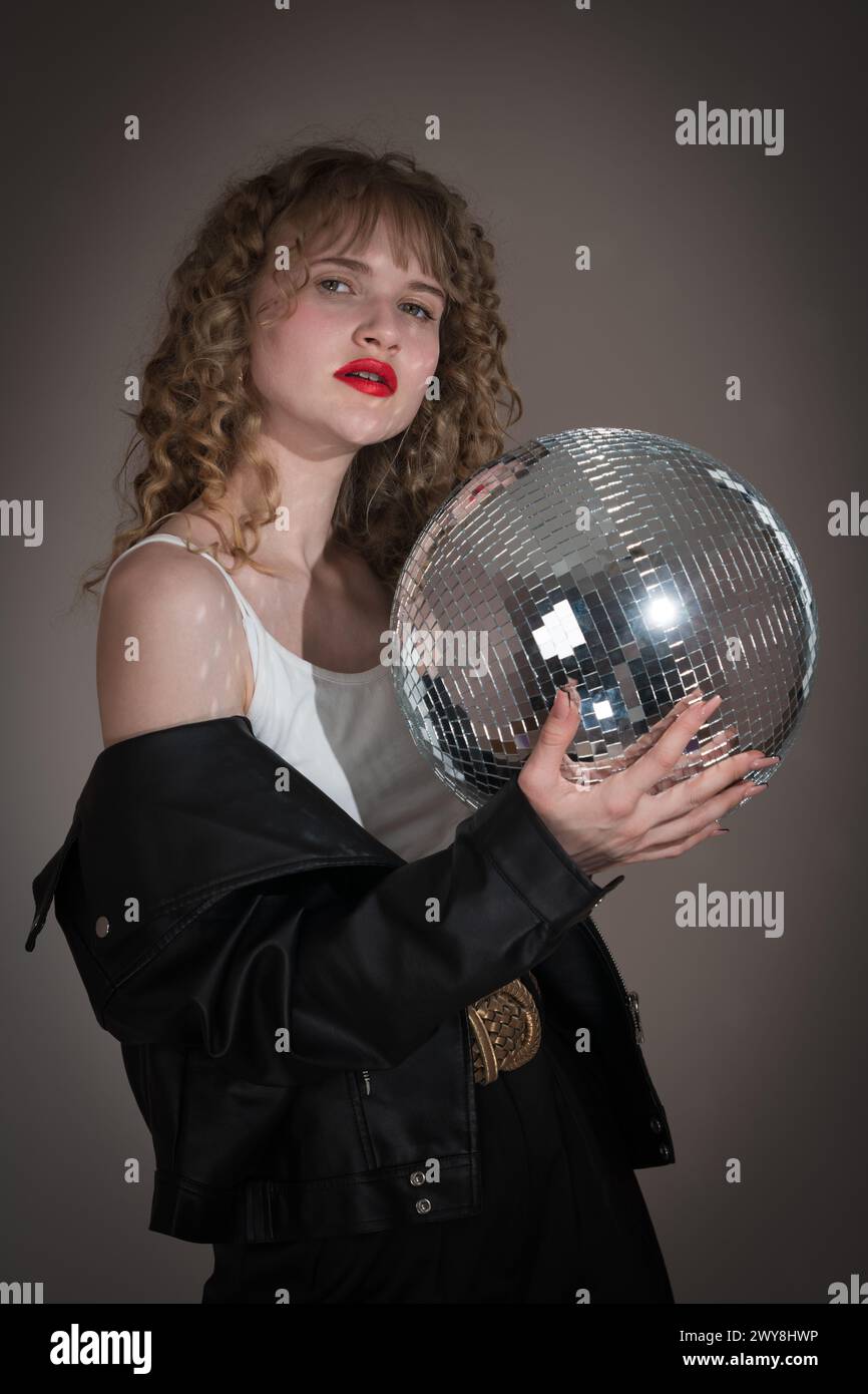 Portrait of woman holding mirror disco ball, looking at camera during ...
